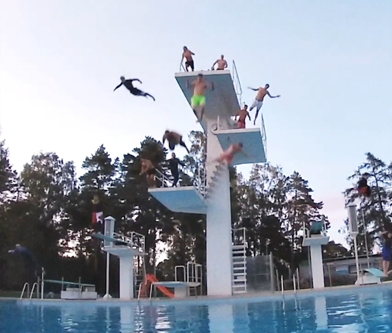 18 Men stand at the top of diving boards by pool, then leap in