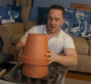 Guy demonstrates how to create a mini heater out of a clay pot to keep ...